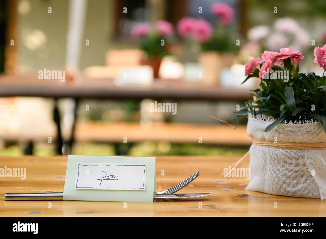 Hand written table name card and cutlery on a wooden table, flowers in ...