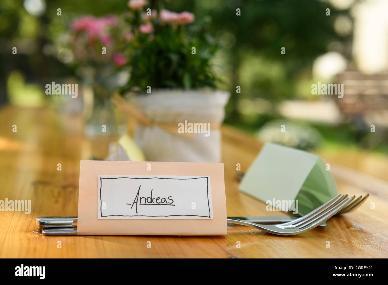Hand written table name card and cutlery on a wooden table, flowers in ...