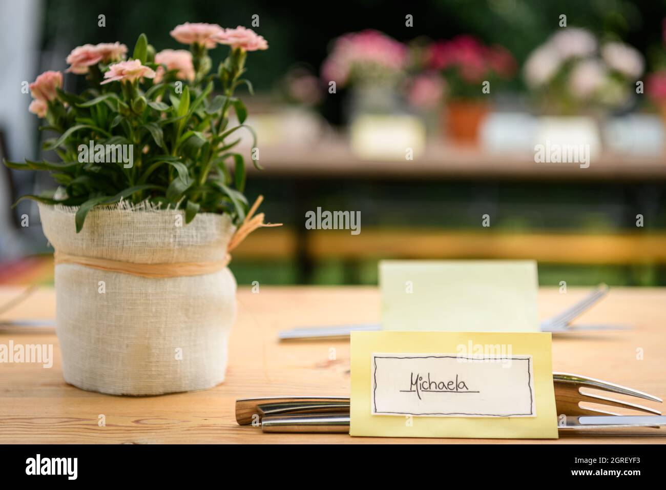 Hand written table name card and cutlery on a wooden table, flowers in ...