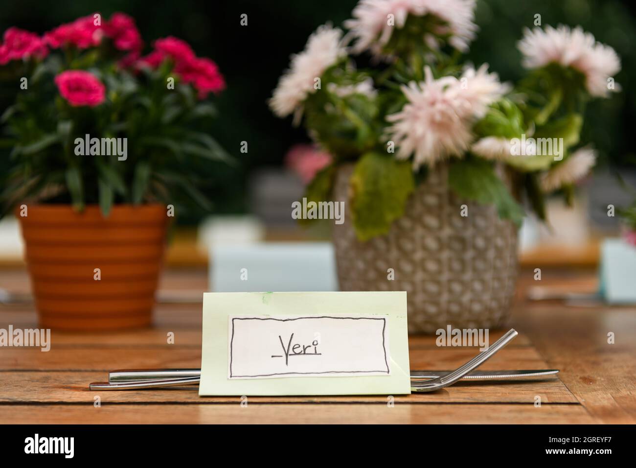 Hand written table name card and cutlery on a wooden table, flowers in ...