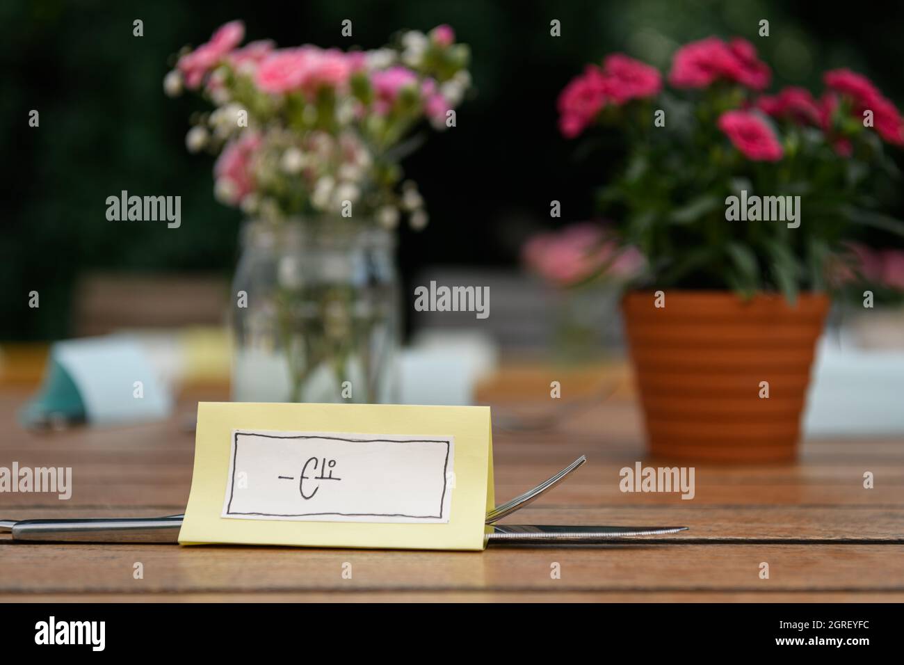 Hand written table name card and cutlery on a wooden table, flowers in ...