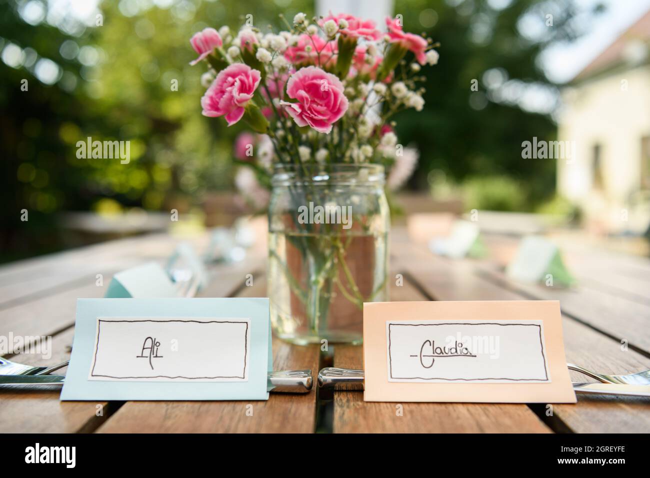Hand written table name card and cutlery on a wooden table, flowers in ...