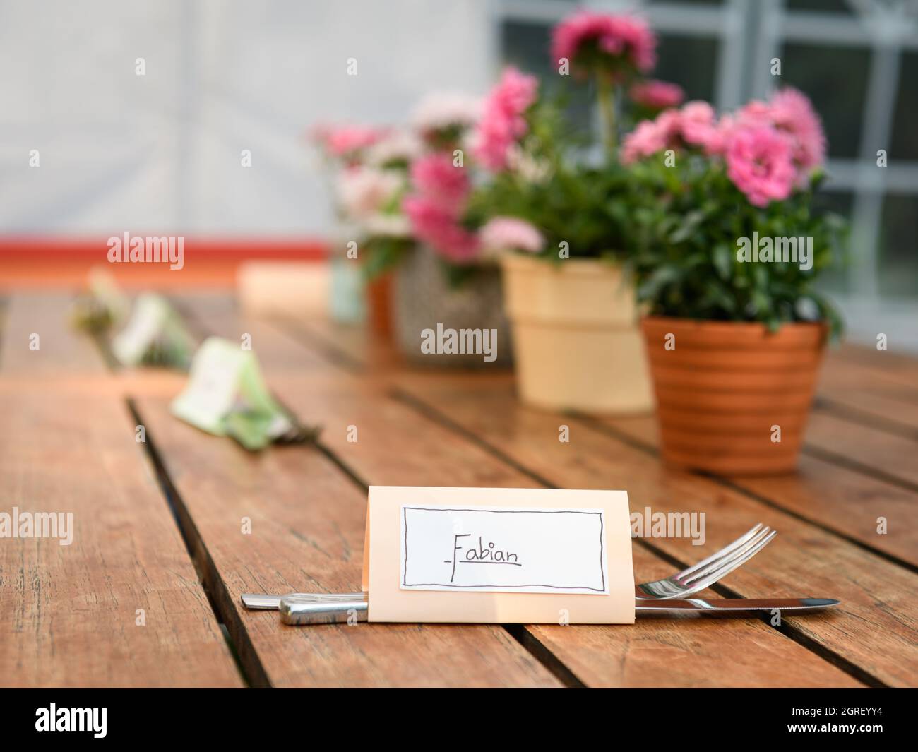 Hand written table name card and cutlery on a wooden table, flowers in ...