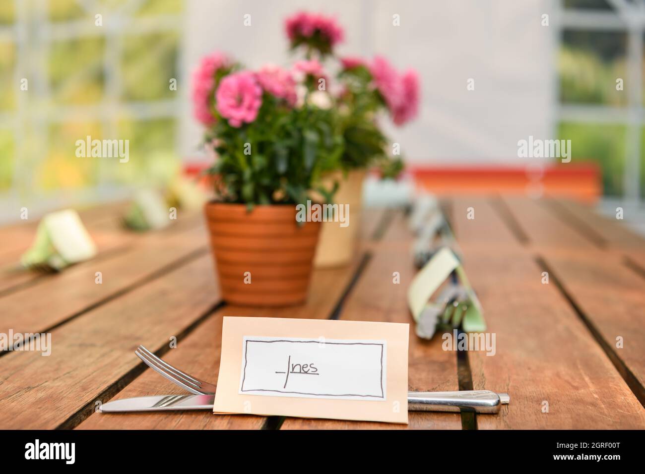 Hand written table name card and cutlery on a wooden table, flowers in ...