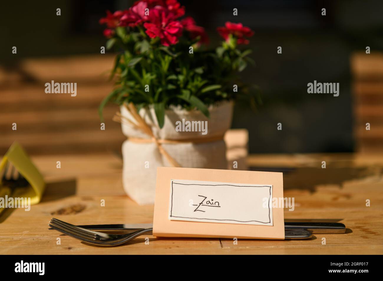 Hand written table name card and cutlery on a wooden table, flowers in ...