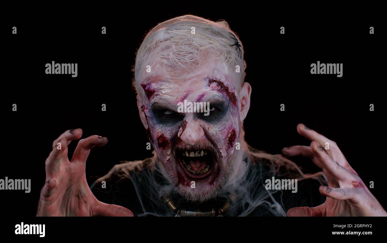Creepy man with Halloween zombie undead bloody wounded make-up, trying ...