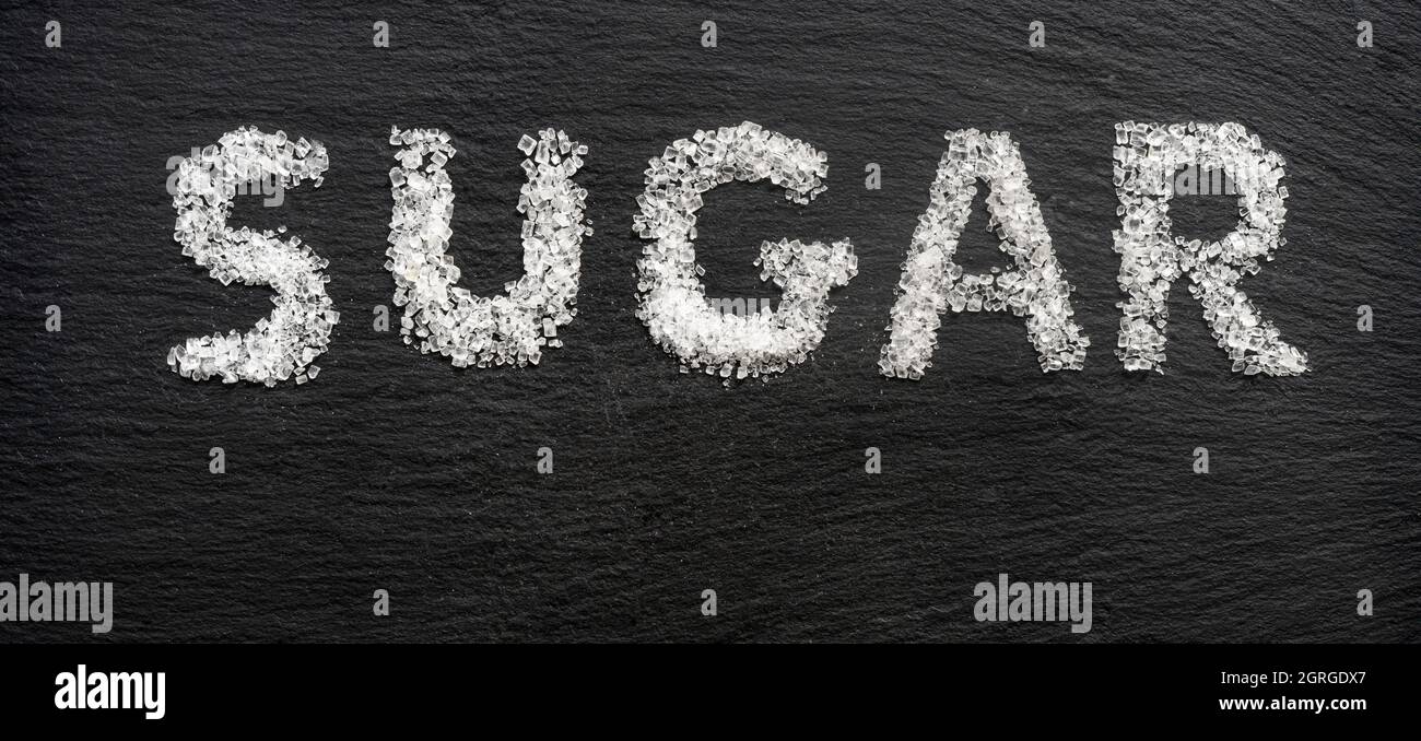 Sugar written with white sugar crystals on black stone tile texture ...