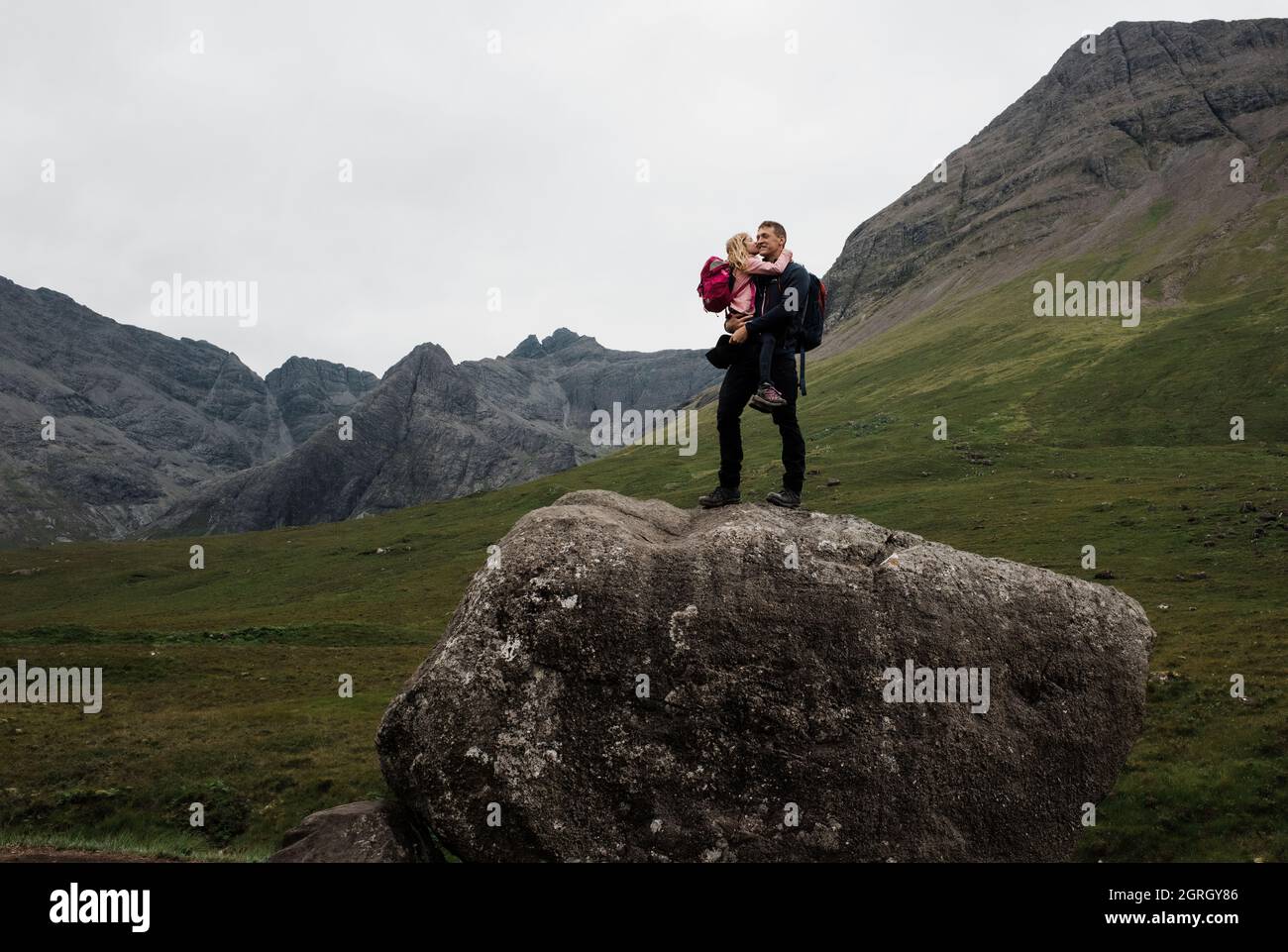 father hugging his daughter after climbing a giant boulder in Scotland ...