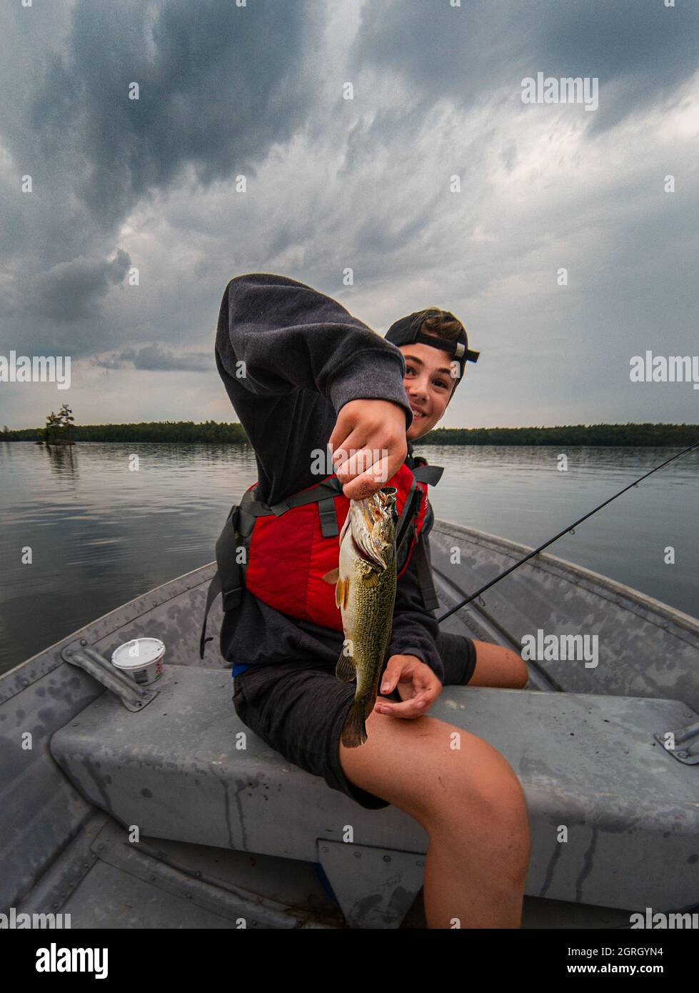 Happy teen boy holding a fish he caught in a boat on a stormy day Stock ...