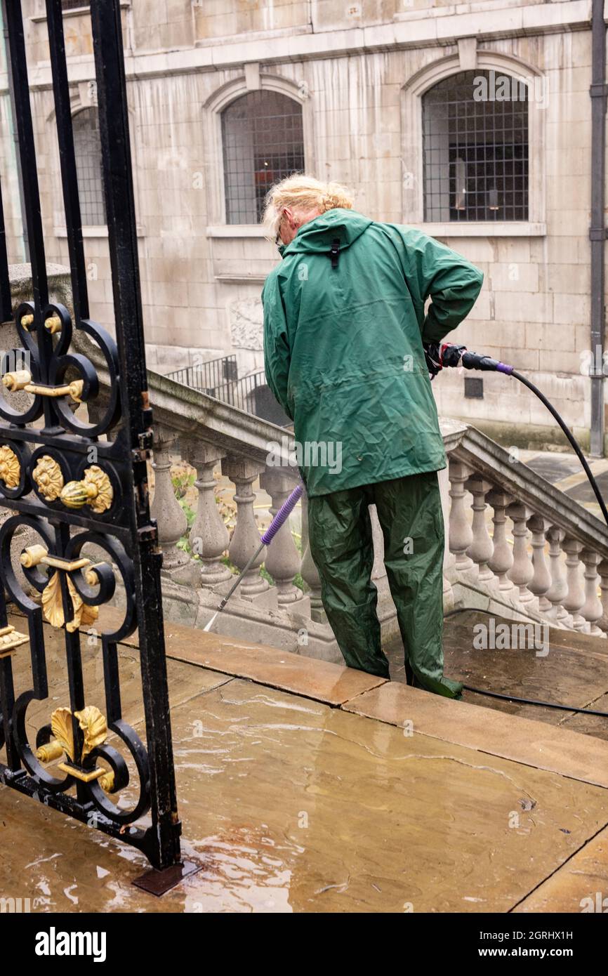 Workman in green overalls water-jetting steps leading in to a large ...