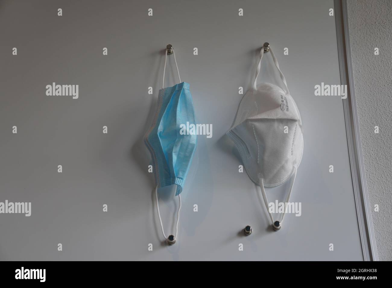 Two used surgical face masks hanging on a white wall during the ...