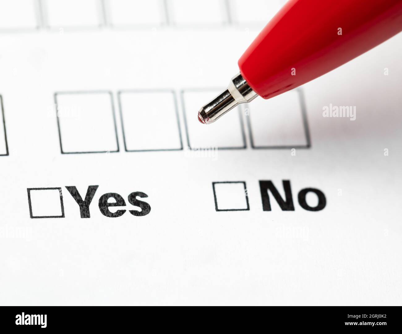Hand holding red ballpoint pen over Yes and No checkboxes in a form ...