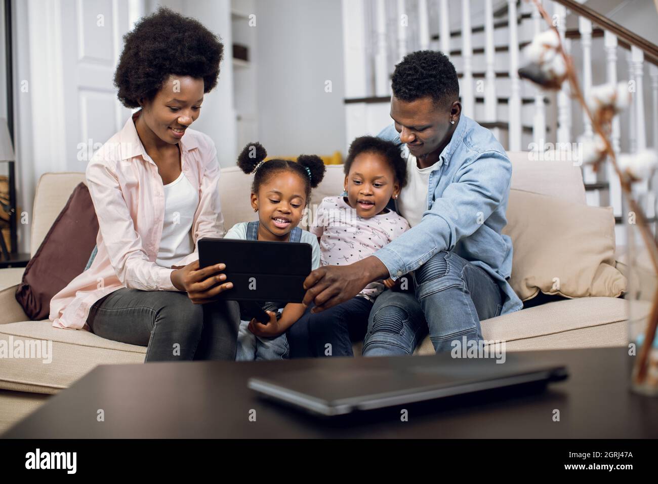 Happy african parents sitting on couch with two pretty daughters and ...