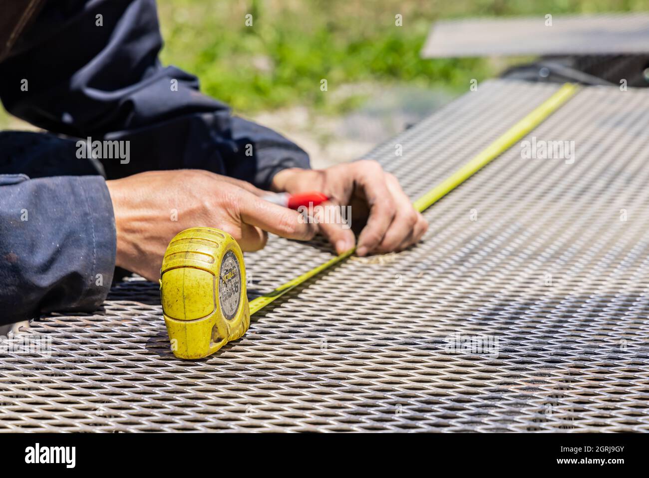 A shot of welder hands holding a pen and a yellow measuring tape ...
