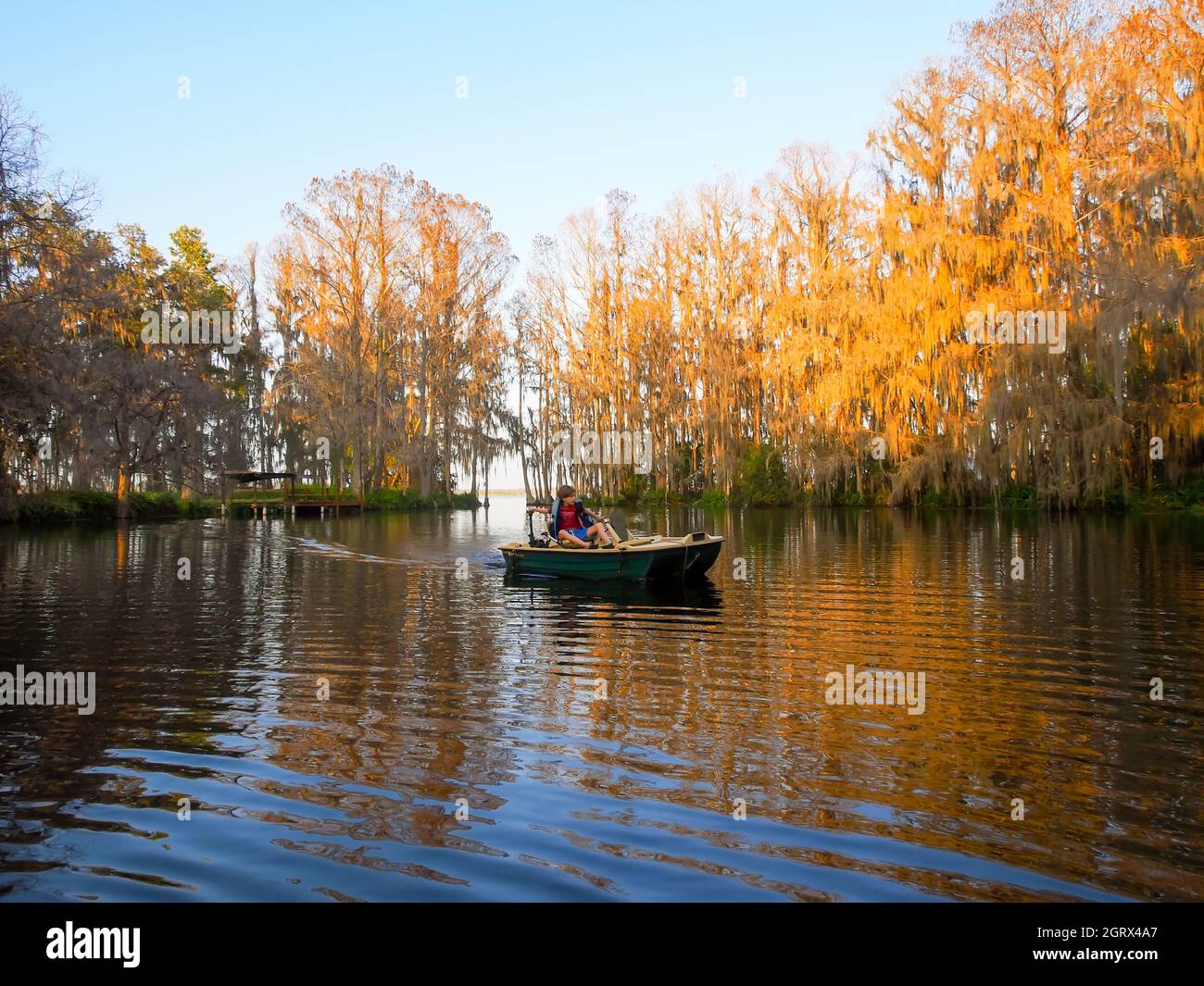 Boy in small motorboat in an inlet off the ocean surrounded by trees ...