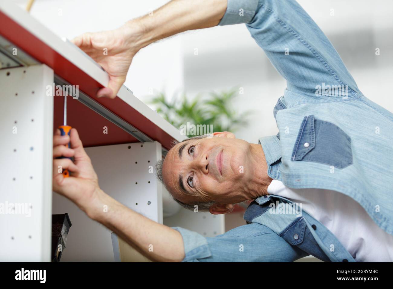 senior man with screwdriver fitting a new kitchen Stock Photo - Alamy