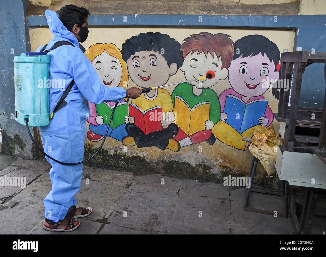 A man wearing a Personal Protective Equipment (PPE) disinfects a wall ...