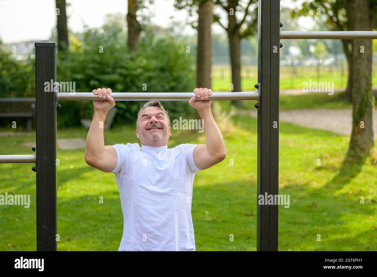 Senior man straining to pull himself up by the arms on a set of ...