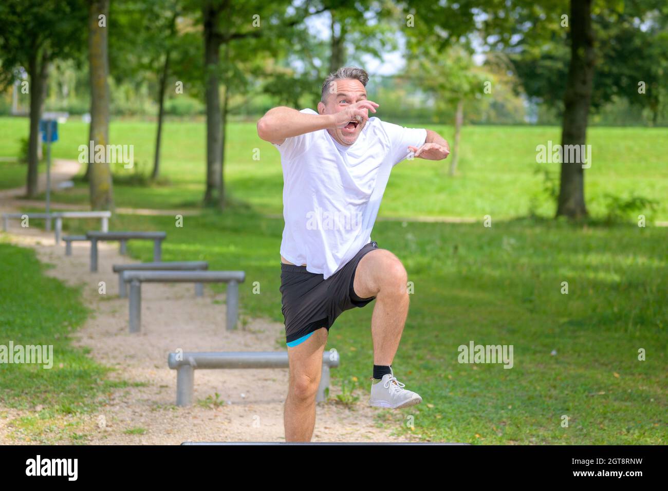 Energetic senior man working out jogging over hurdles on a footpath in ...