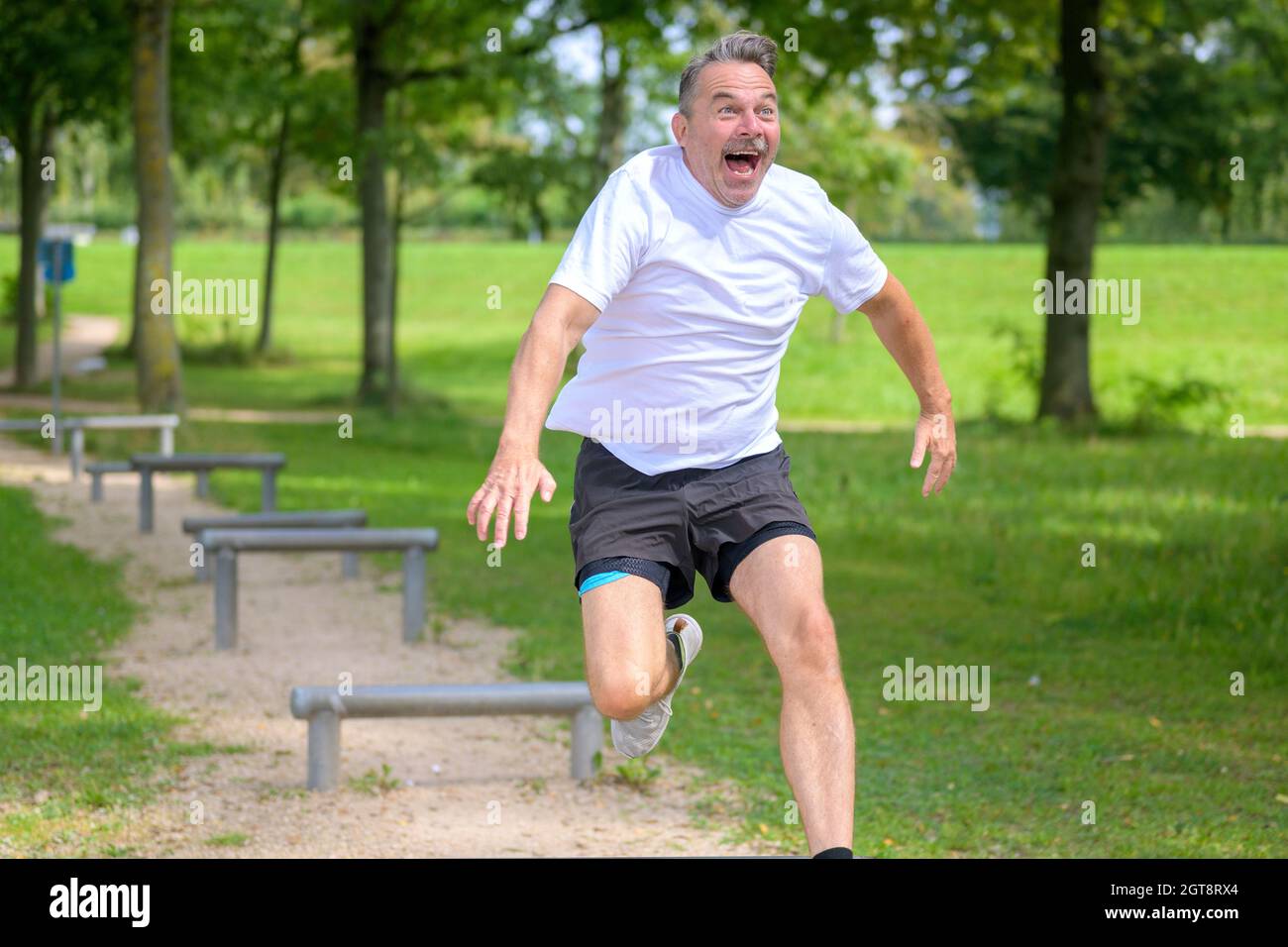 Man using low bars in a park as hurdles as he runs along a footpath in ...