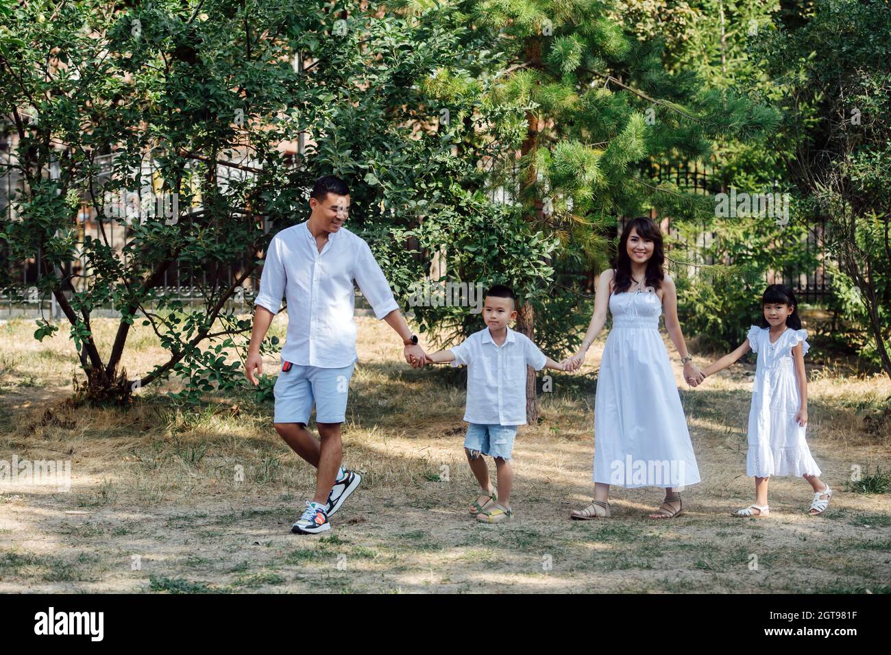 Happy asian family in white clothes having a walk on a grass in a park ...