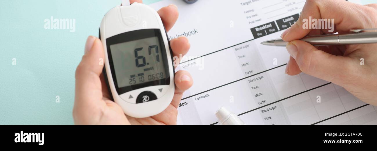 Person holds glucometer with blood sugar readings and makes notes in ...