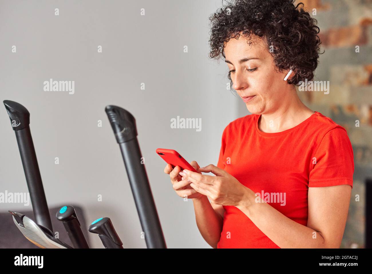Woman exercising at home on cross training elliptical using mobile ...