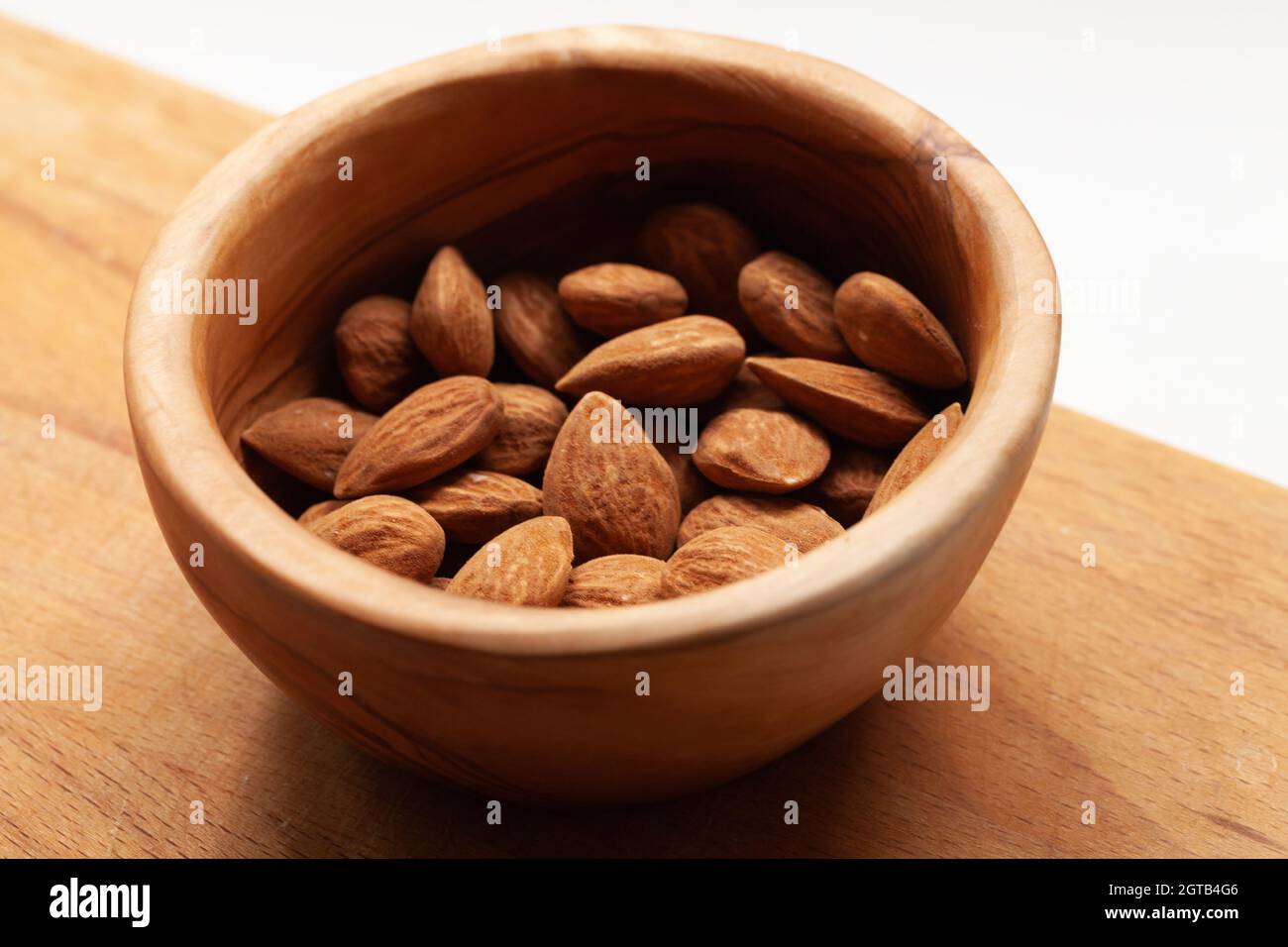 A wooden bowl full of raw almond nuts stands on a cutting desk, close ...