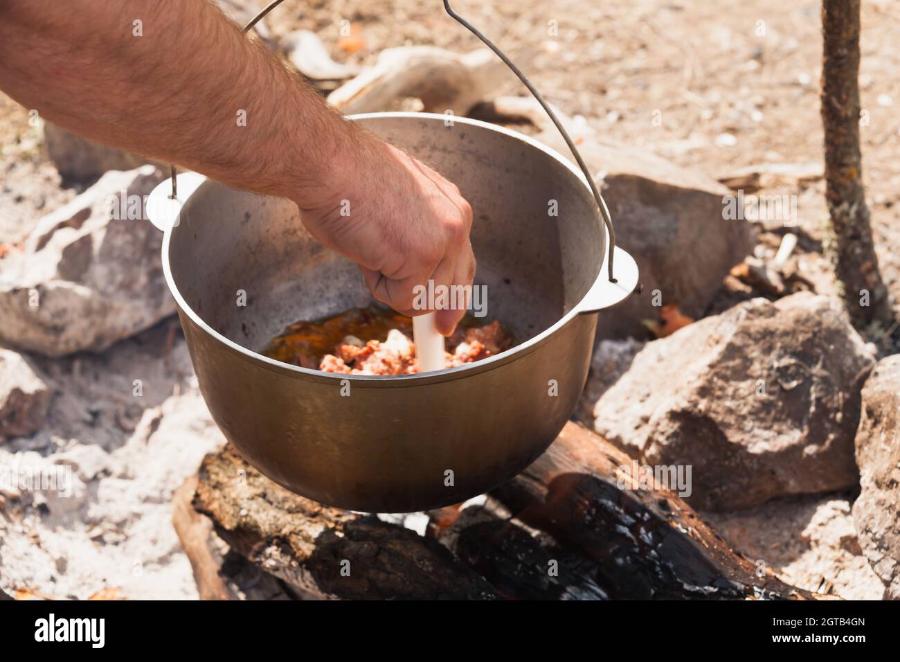 Male hand mixing soup in a cauldron. Preparing of a meal on open fire ...