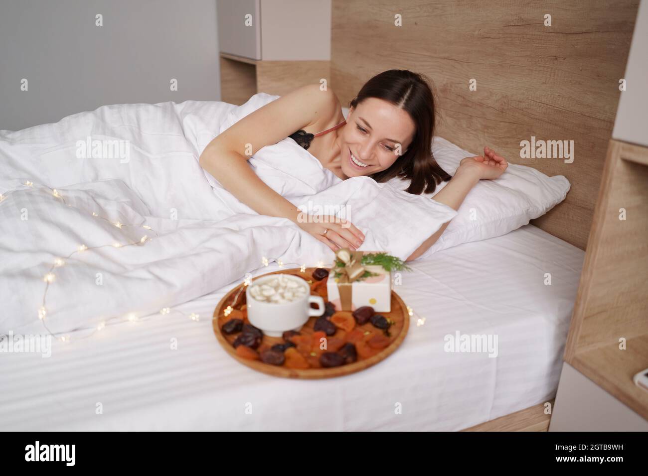 Woman awake on the bed with present and coffee with marshmallows ...