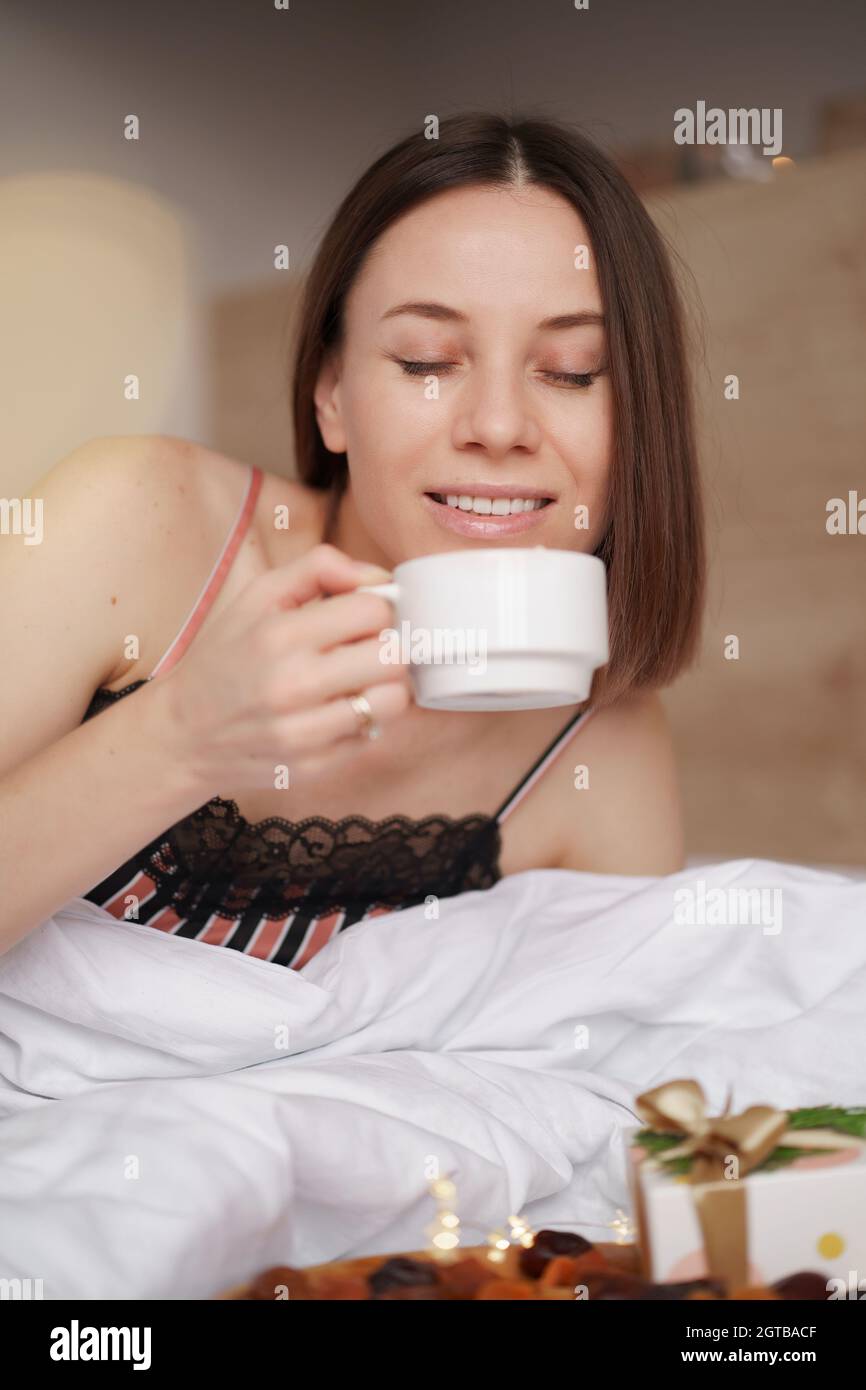 Woman awake on the bed with present and coffee with marshmallows ...