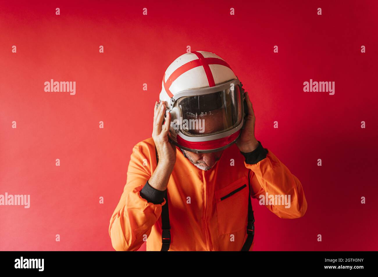 Astronaut with an orange space suit taking off his helmet on a red ...