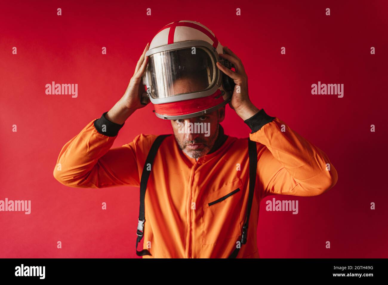 Astronaut with an orange space suit taking off his helmet on a red ...