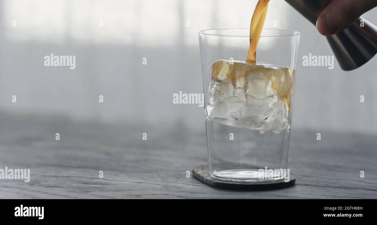 coffee pour over ice cube in tumbler glass on black wood table, wide ...