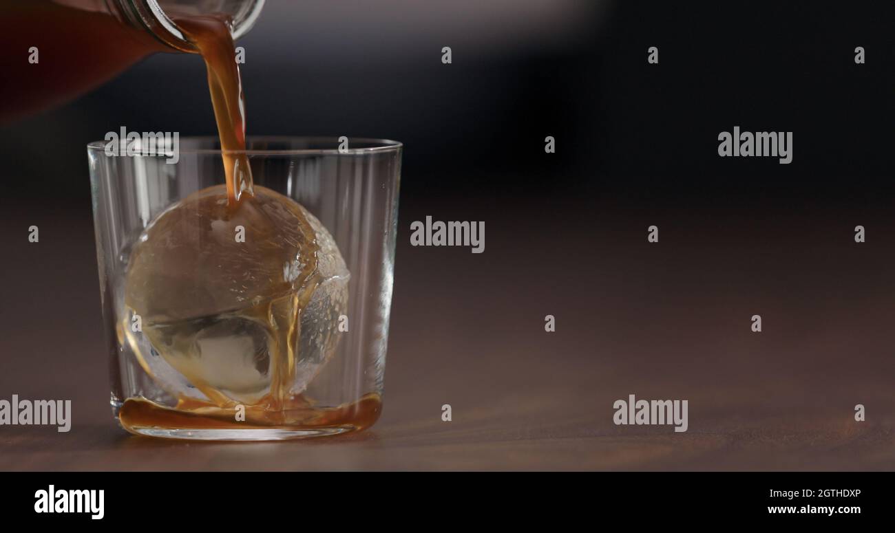 coffee pour over ice ball in tumbler glass on black walnut table, wide ...
