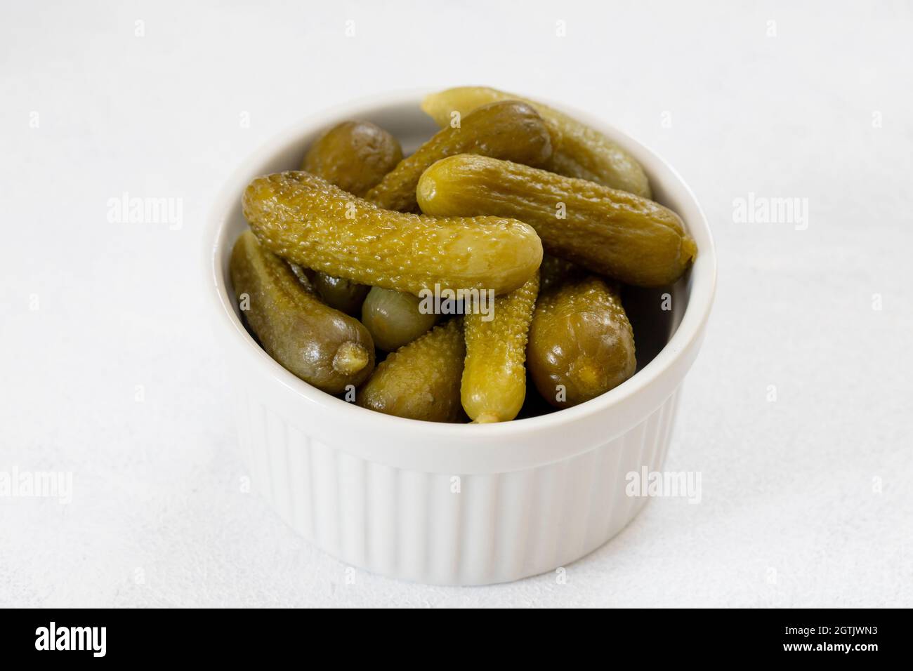 Crunchy pickled cornichons in a white ceramic bowl. Marinated green ...