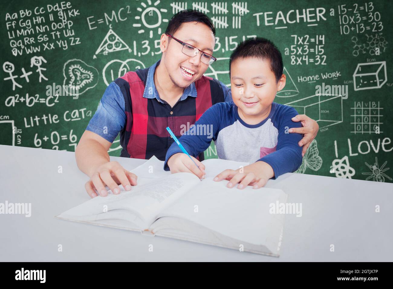 Smiling Teacher Teaching Boy At Desk Against Green Board With Text ...