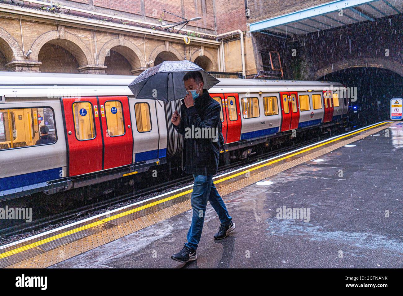 LONDON, UK. 2 OCTOBER, 2021. A commuter shelters under an umbrella at ...