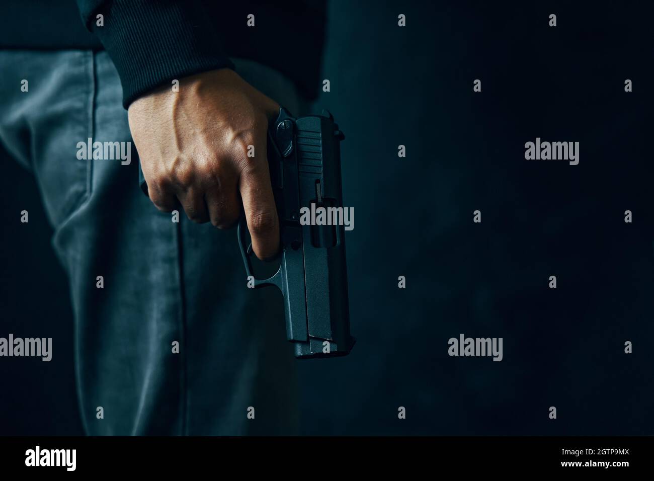 Man stands with gun lowered. Person in jeans holds firearm in his hand ...