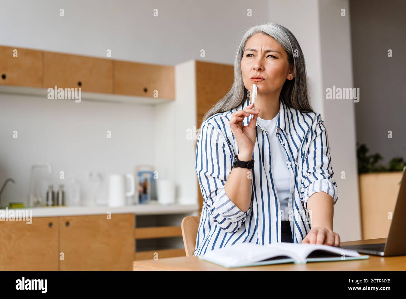Serious white-haired mature woman writing down notes working with ...