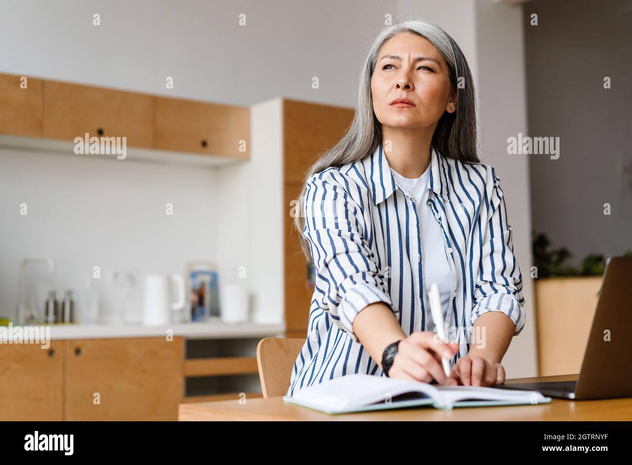 Serious white-haired mature woman writing down notes working with ...