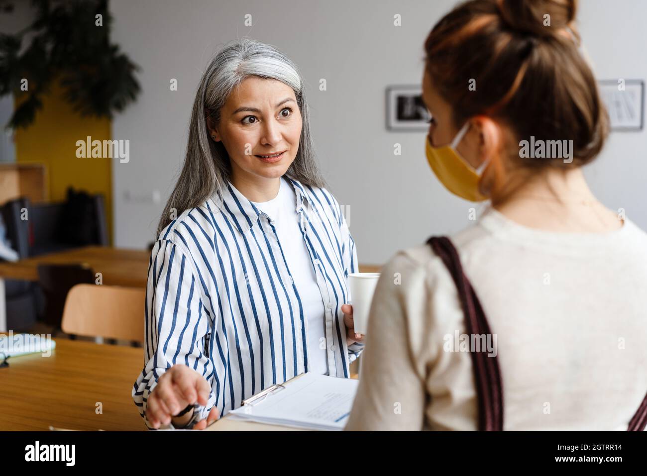 Two employee standing in social distance wearing face mask talking in ...