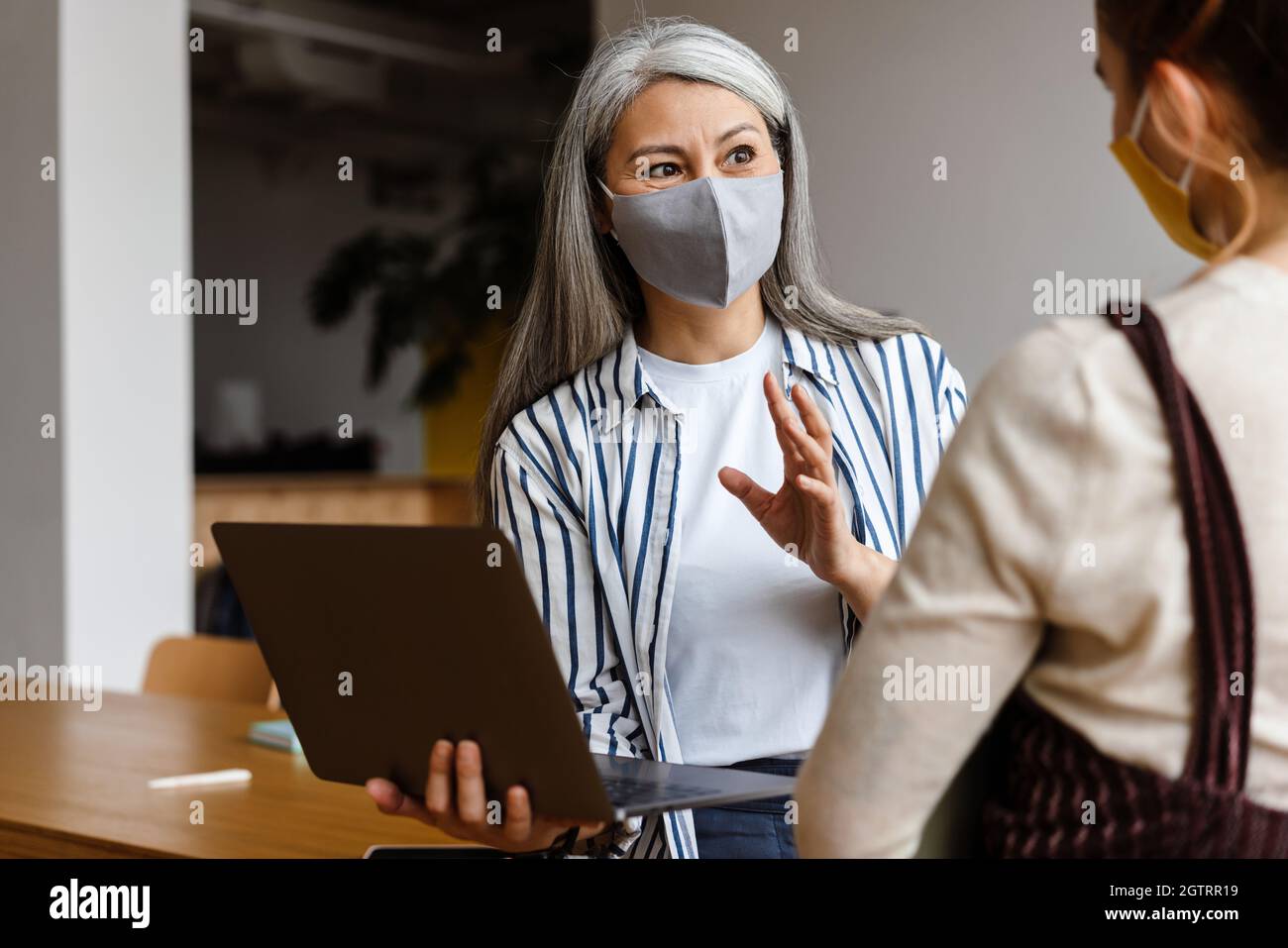 Two employee standing in social distance wearing face mask talking in ...