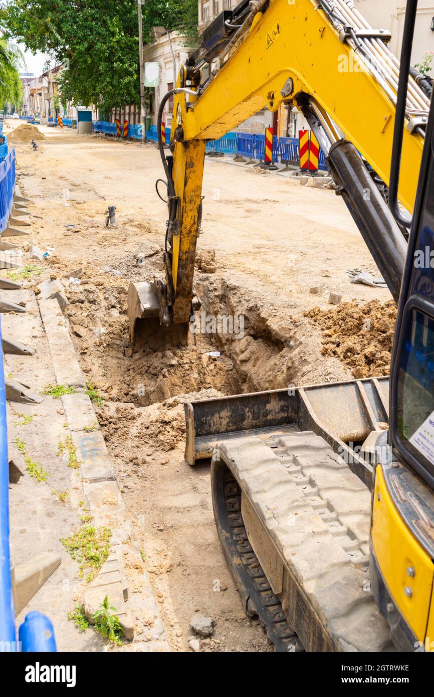 Yellow excavator digging a trench in the road Stock Photo - Alamy