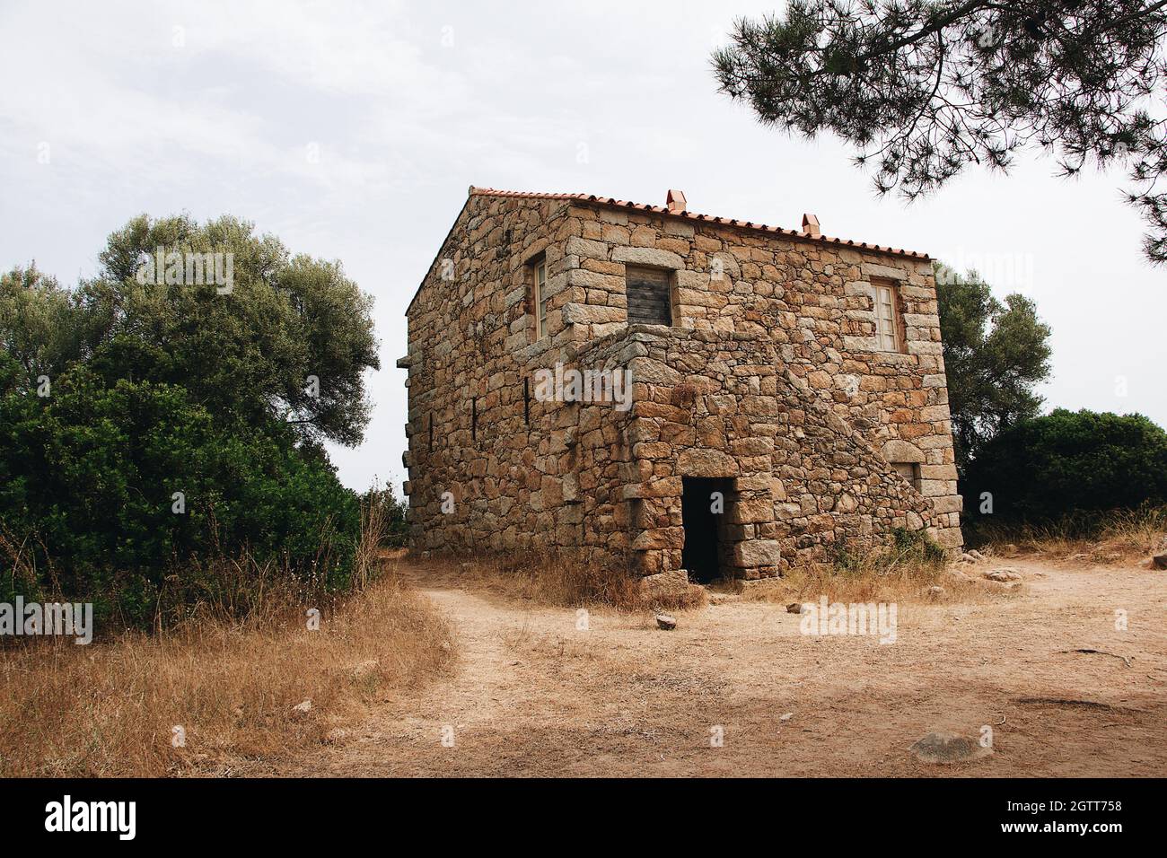 Old abandoned stone building surrounded by greenery under a cloudy sky ...