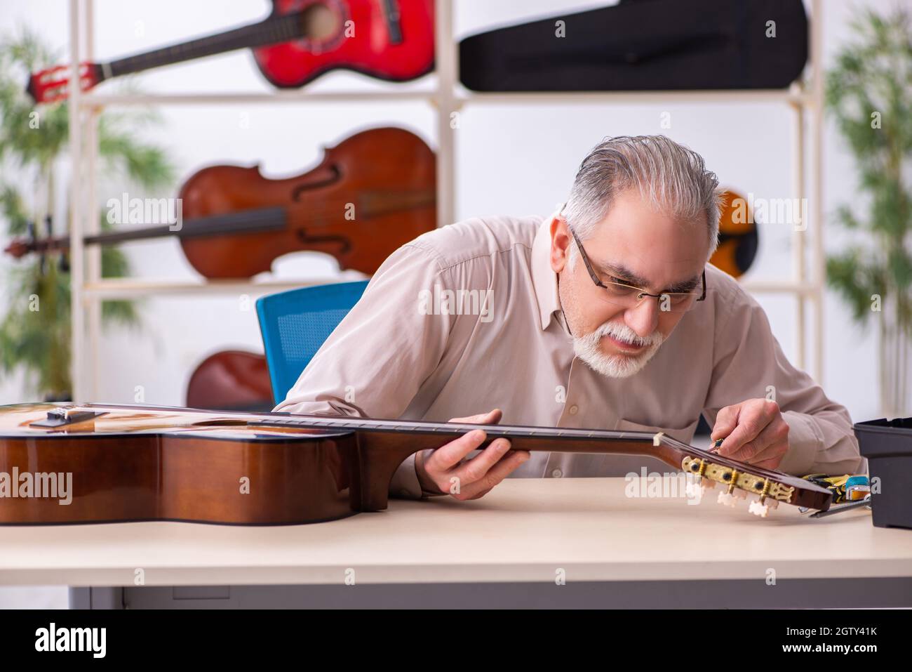 Old repairman repairing musical instruments at workplace Stock Photo ...