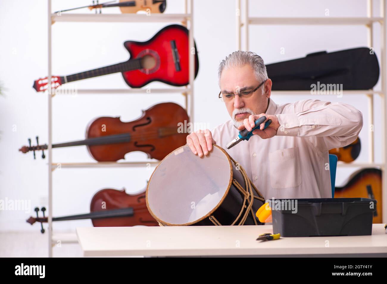 Old repairman repairing musical instruments at workplace Stock Photo ...