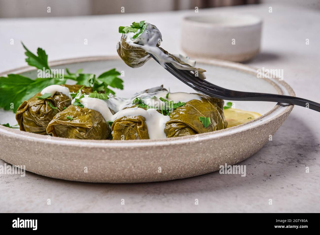 Close up dolma in light plate with with sour cream, on black fork ...