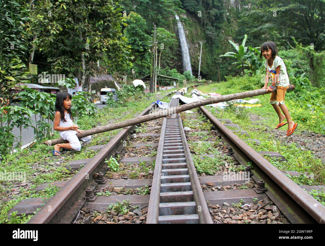 Two young girls playing on old train tracks using an old wooden pole as ...