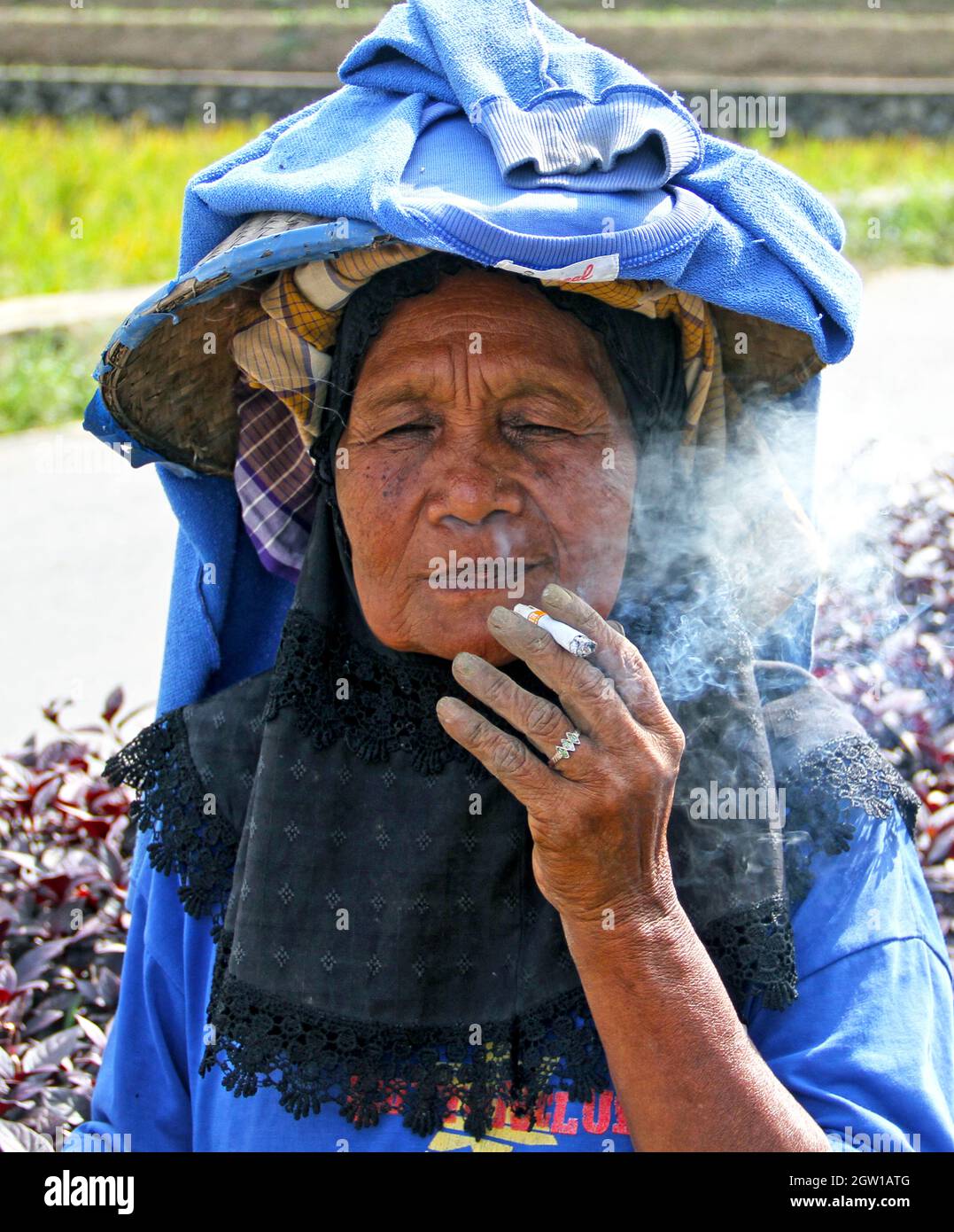 An elderly Minangkabau rice farmer woman smoking a cigarette near the ...